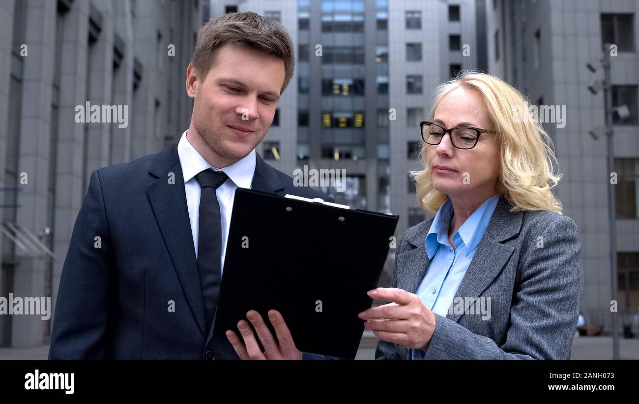 Aged female boss checking young employee report, business partners ...