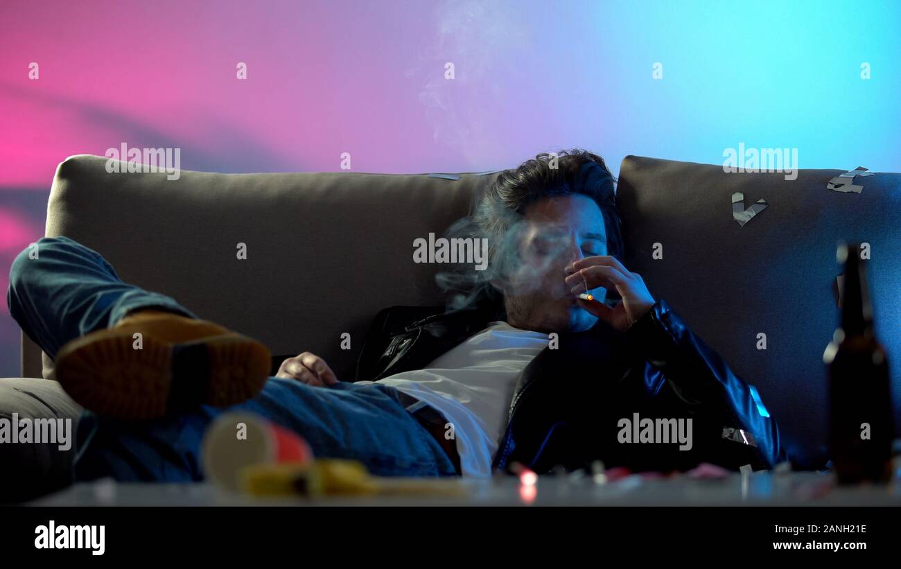 Careless drunk man smoking cigarette and relaxing on sofa at nightclub ...