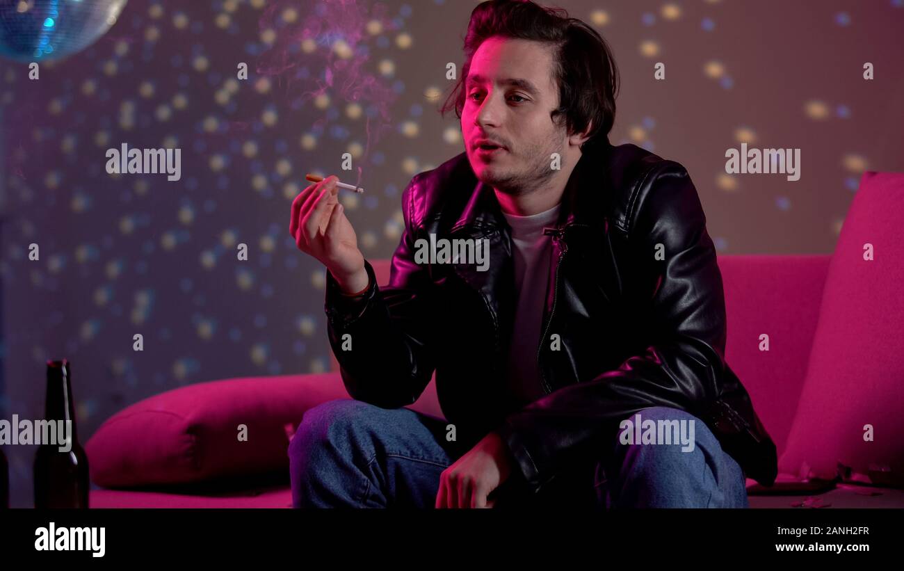Relaxed male smoking cigarette, chilling out at private disco party ...