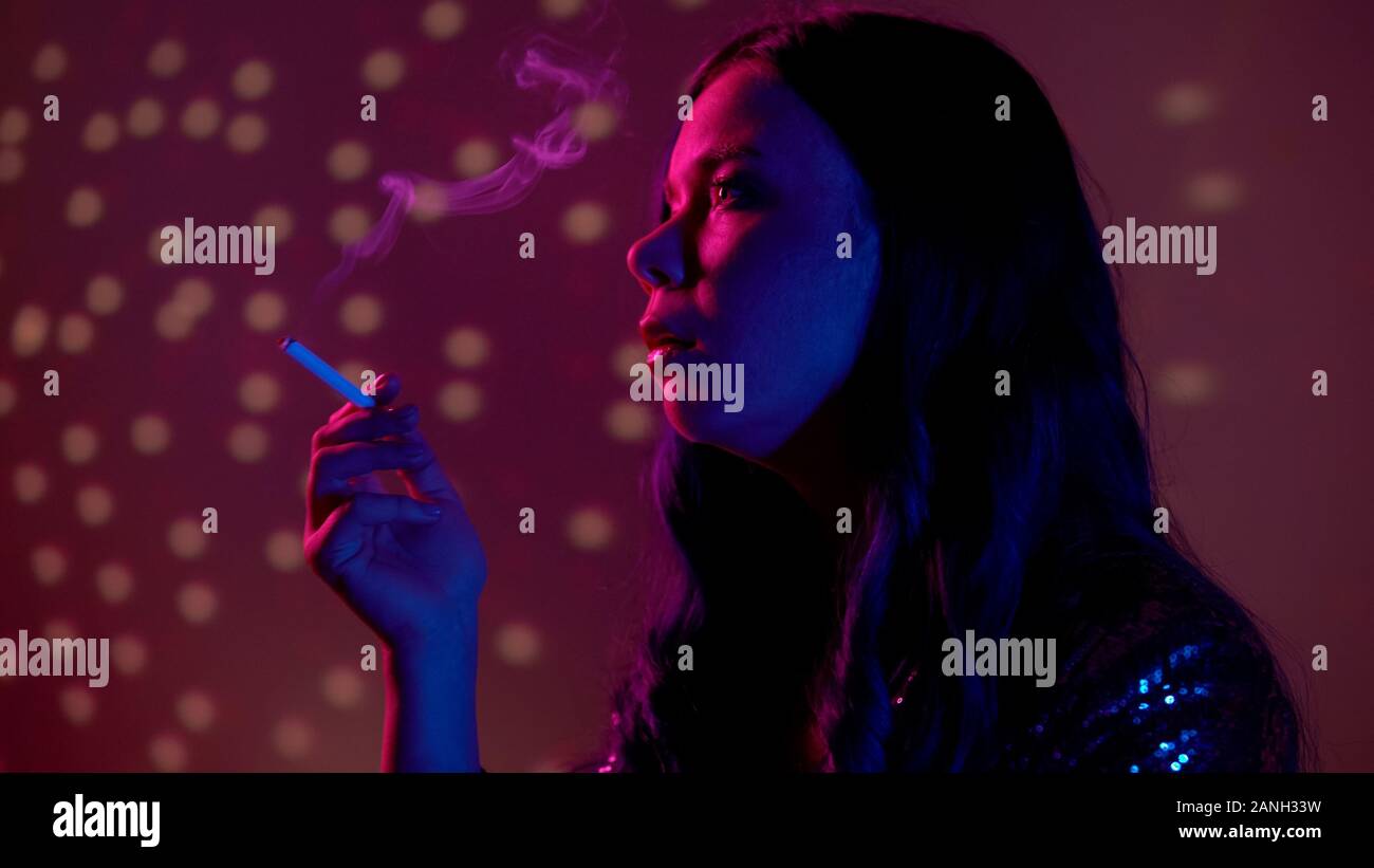 Serious young woman smoking cigarette at nightclub party, unhealthy ...