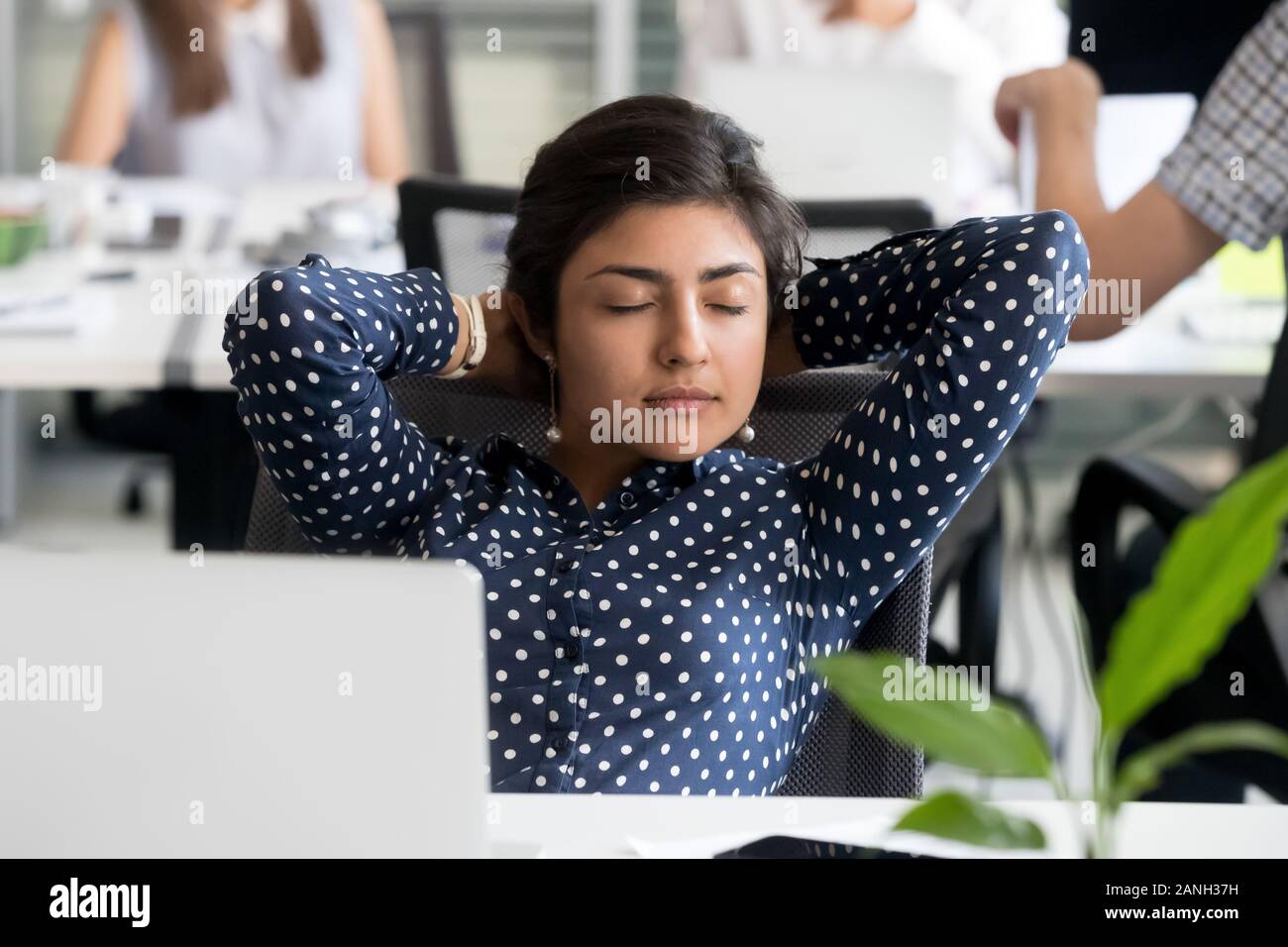 Calm young indian office worker relax in chair hands over head taking ...
