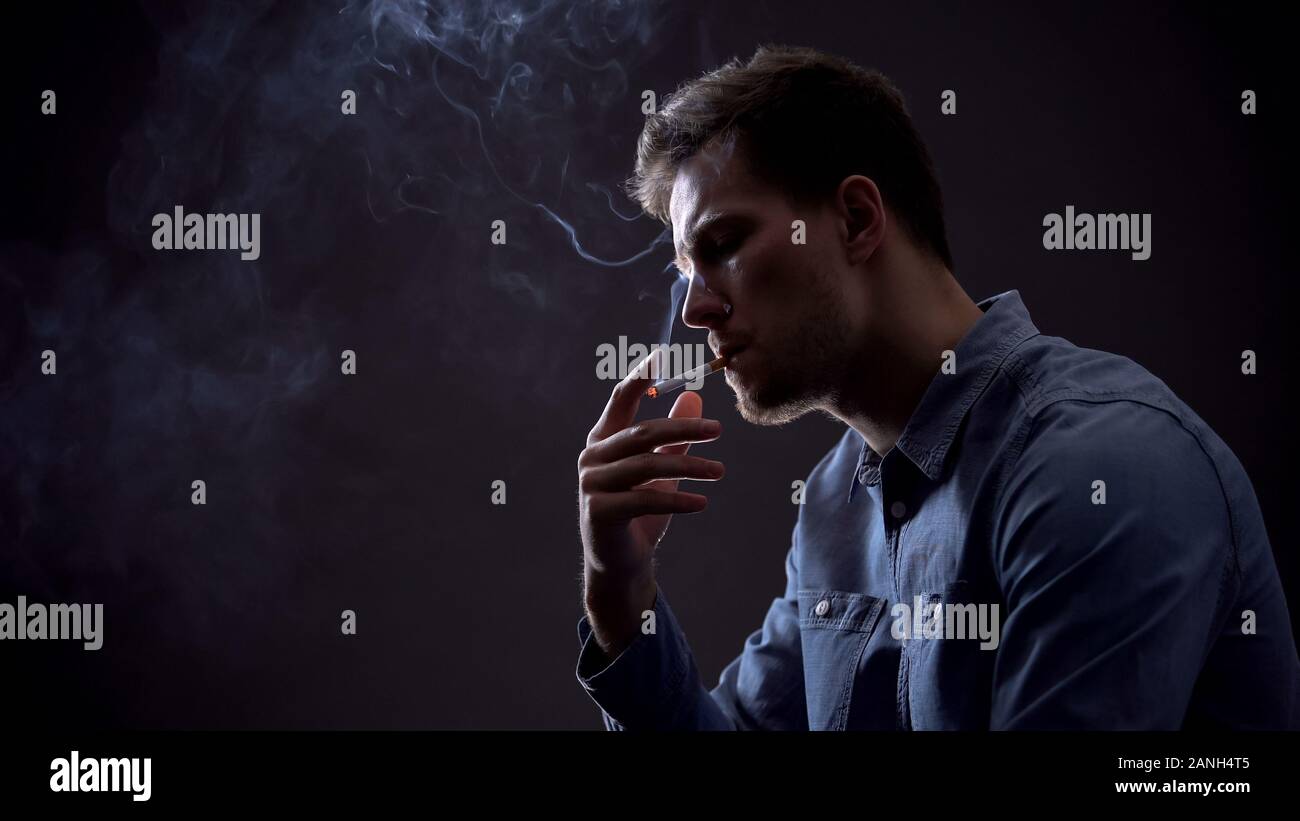 Depressed man smoking isolated on dark background, thinking about life ...