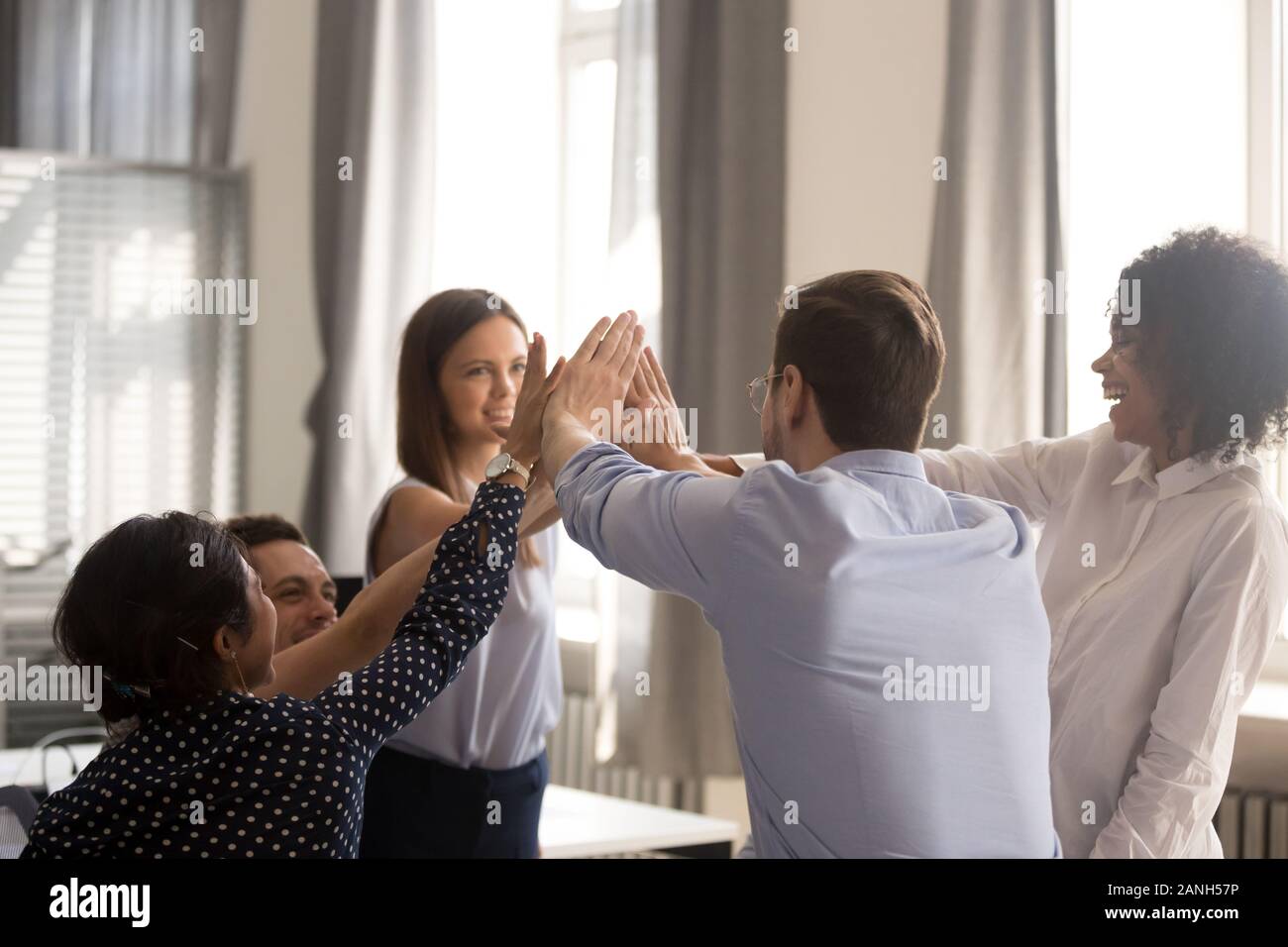 Excited multiracial young coworkers laugh giving high five involved in ...