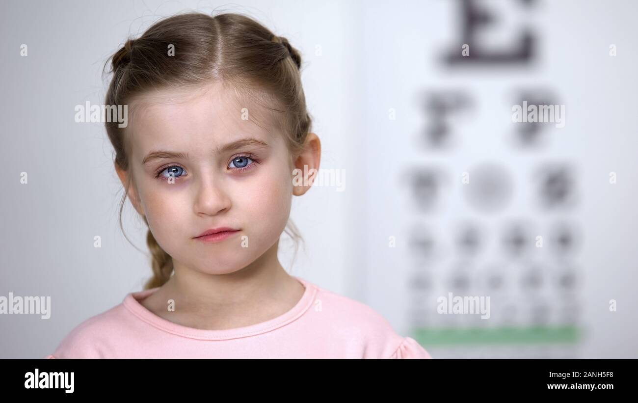 Sad little girl with red eyes on reception at ophthalmologist, vision ...