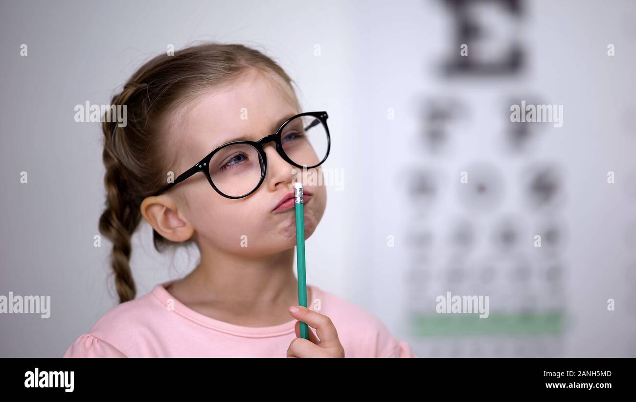 Pensive smart girl wearing glasses, testing vision with eye chart in ...