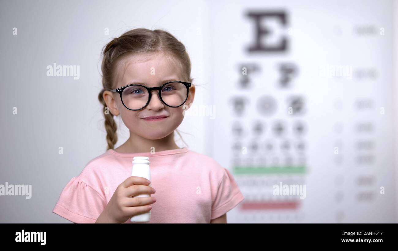 Cheerful kid in glasses drinking delicious vitamin syrup to improve ...