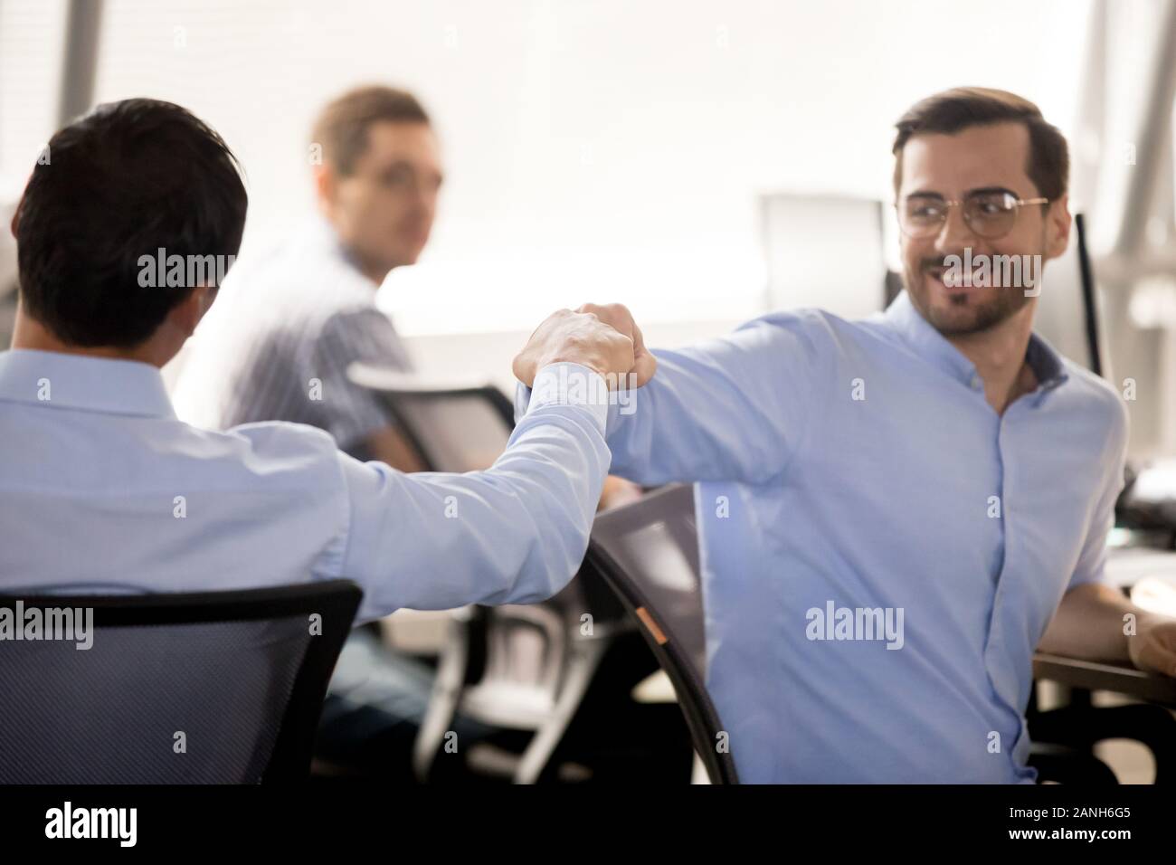 Smiling male colleagues give fists bump make gesture greeting meeting ...