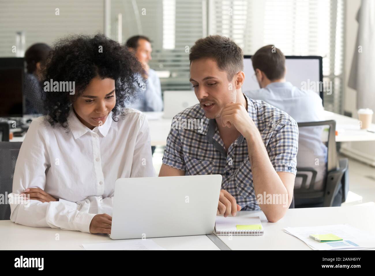 Multiracial millennial colleagues sit at office desk working on laptop ...