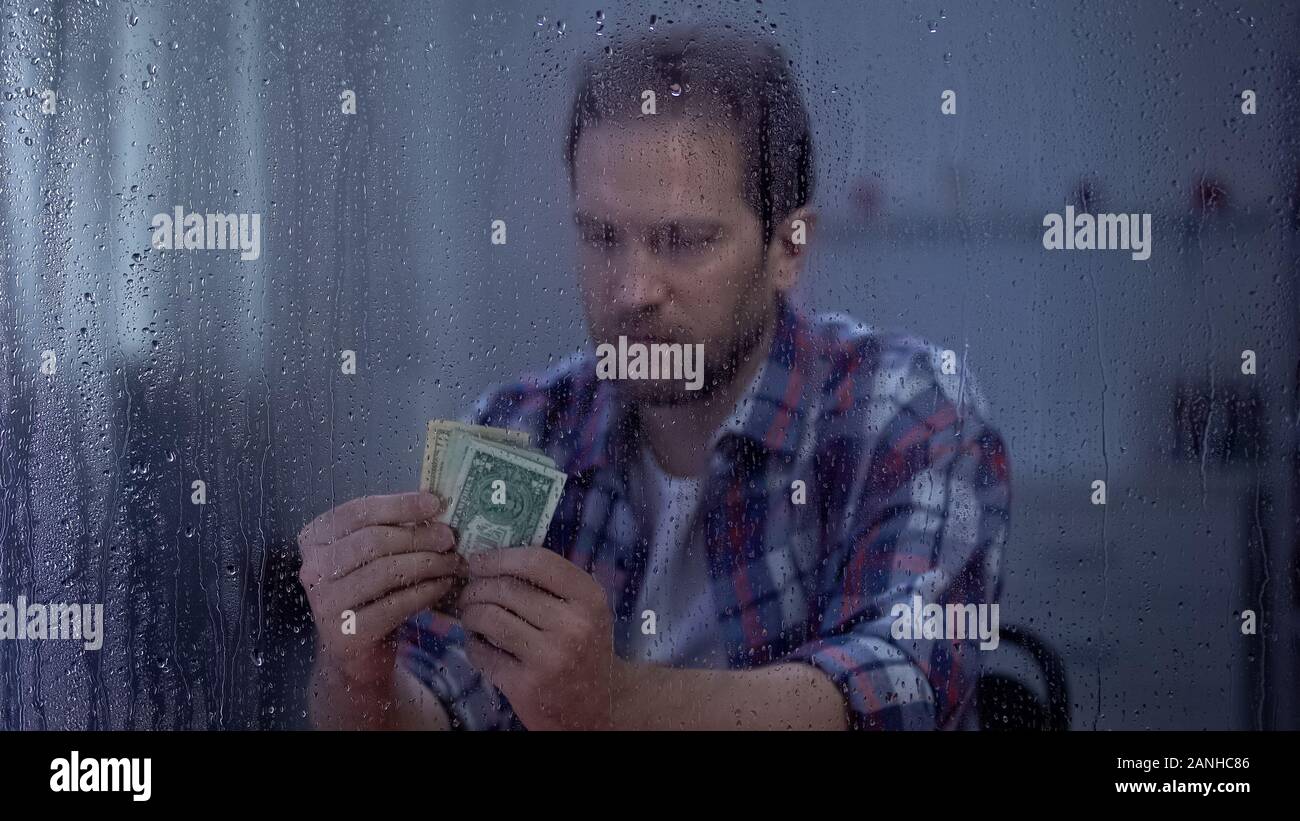 Middle-aged man counting money behind rainy window, poor budget ...