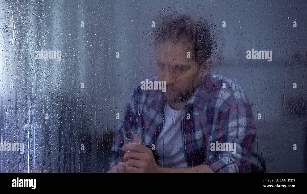 Drunk man with glass of vodka behind rainy window, alcohol addiction ...