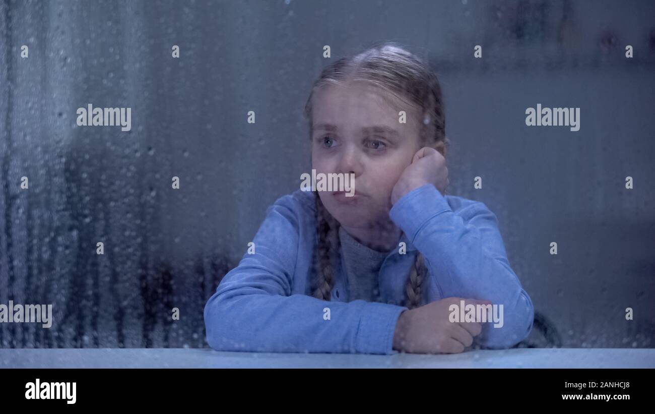 Lonely girl looking at window in rainy weather, waiting parents from ...