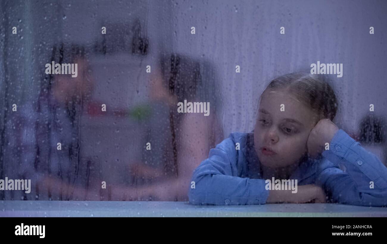Upset girl sitting behind rainy window, listening parents quarrel ...