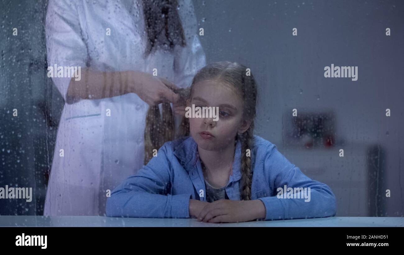 Nanny braiding little girls hair behind rainy window, care in orphanage ...