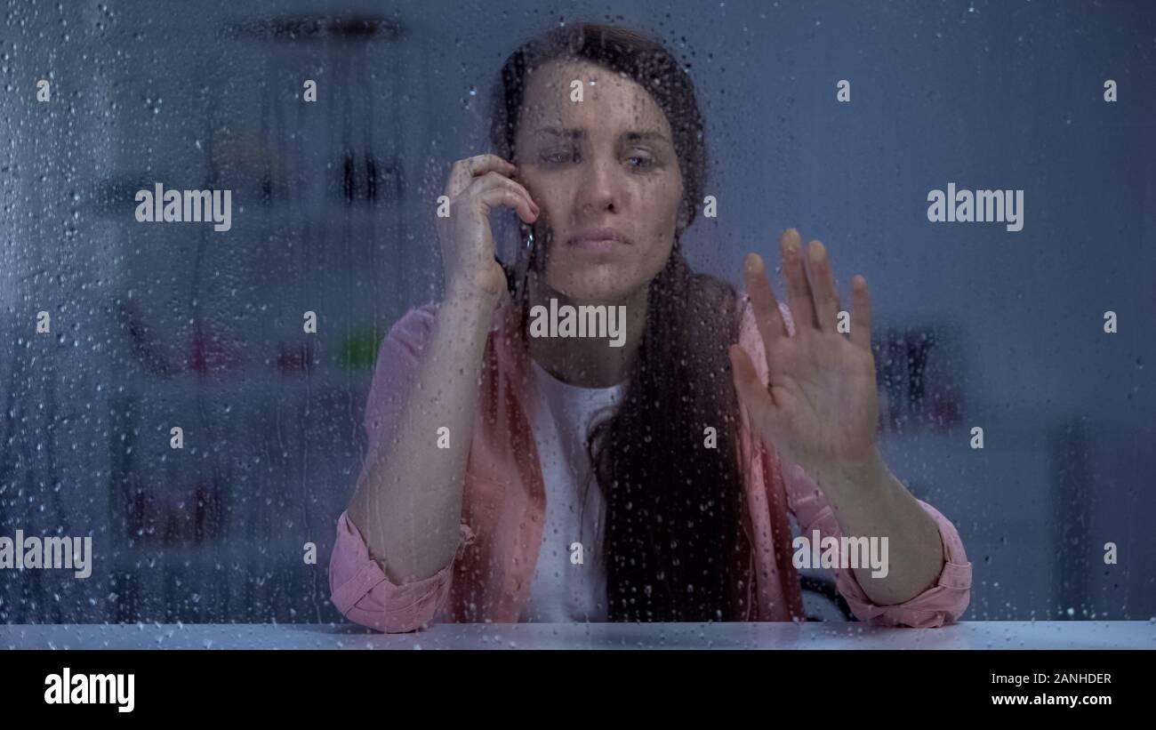Woman talking phone and looking through rainy window, waiting husband ...