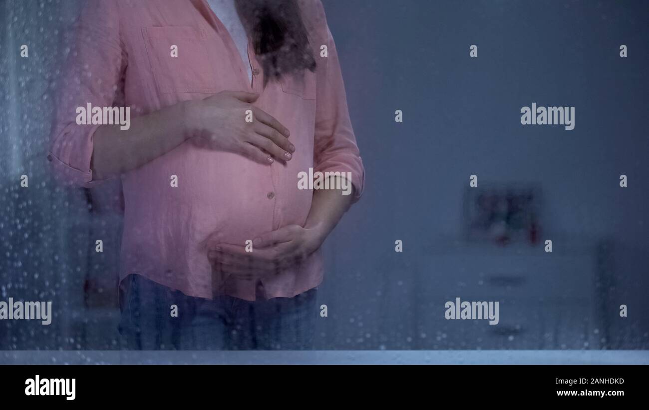 Pregnant woman stroking tummy behind rainy window, baby expectation ...