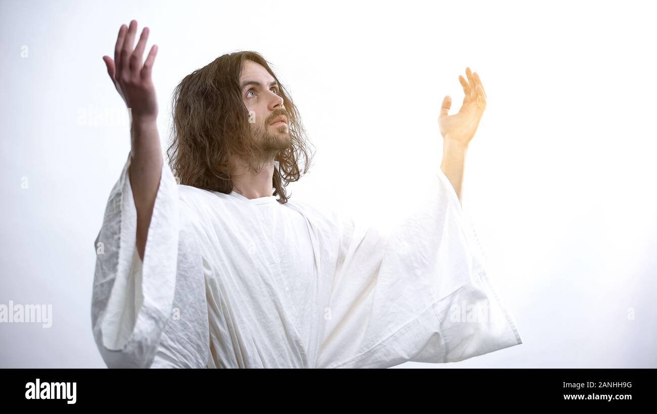 Saint man in robe raising hands to light, praying to God, religious ...