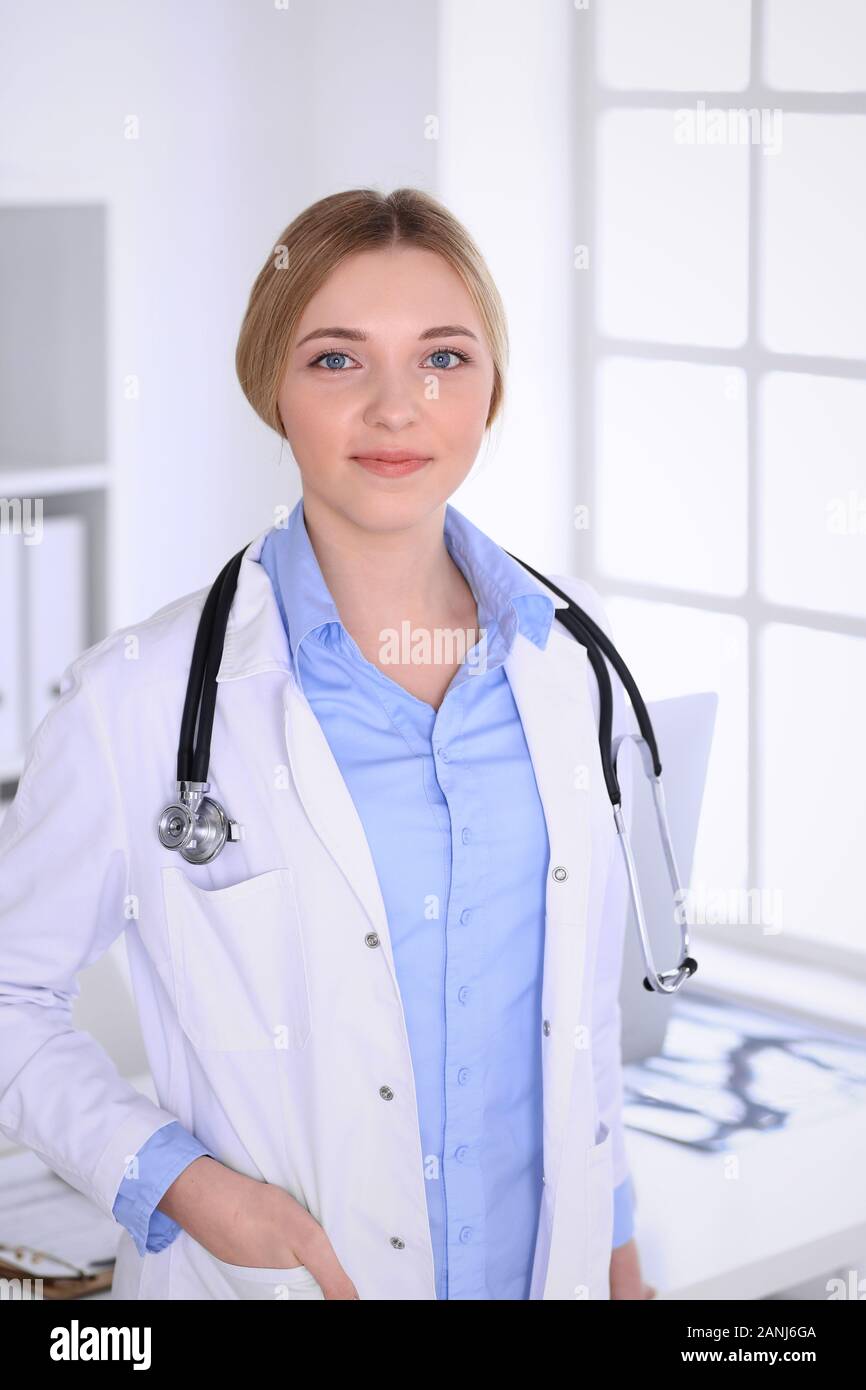 Young woman doctor at work in hospital looking at camera. Blue colored ...