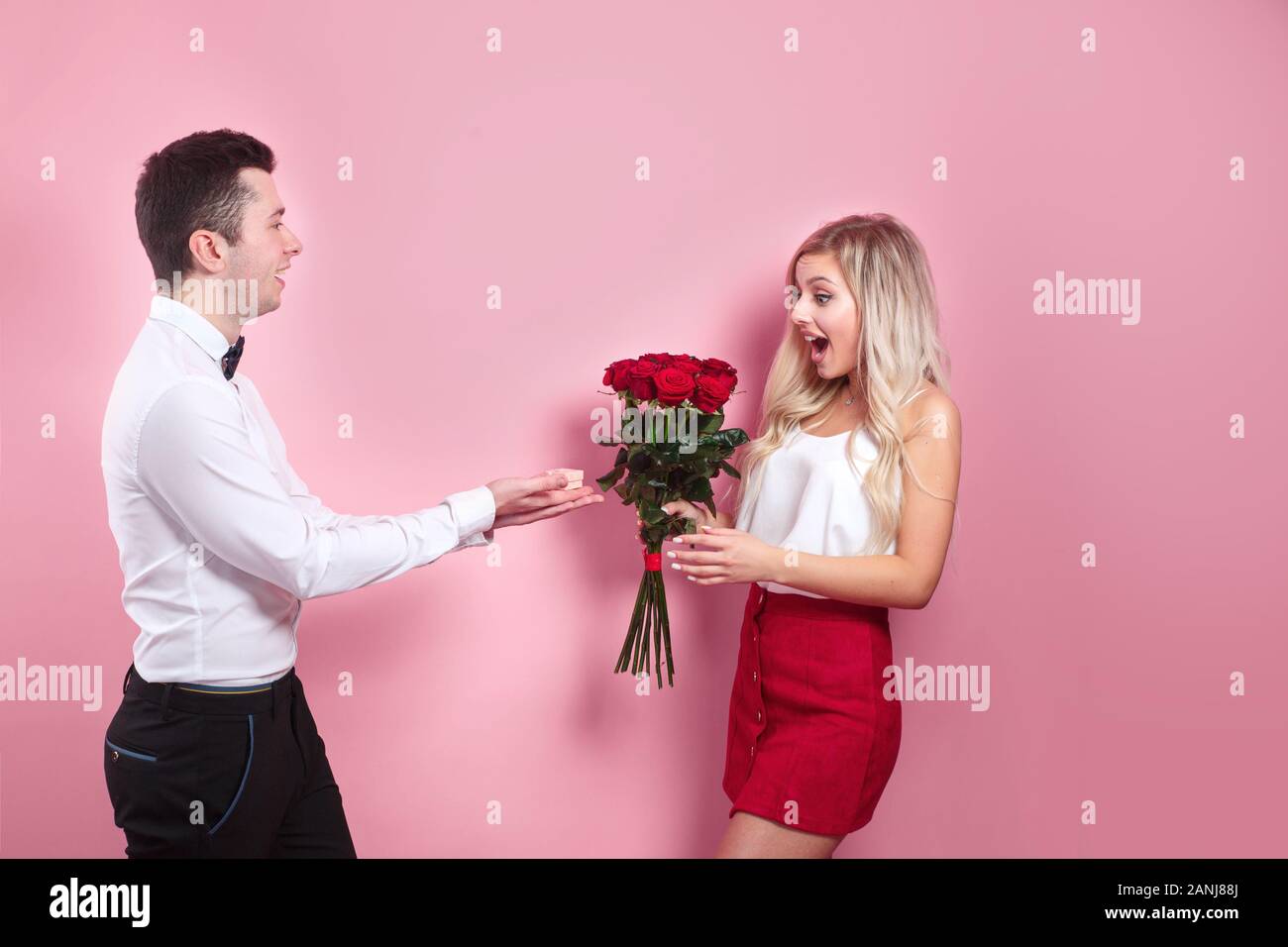 Handsome man proposing a beautiful woman to marry him on pink ...