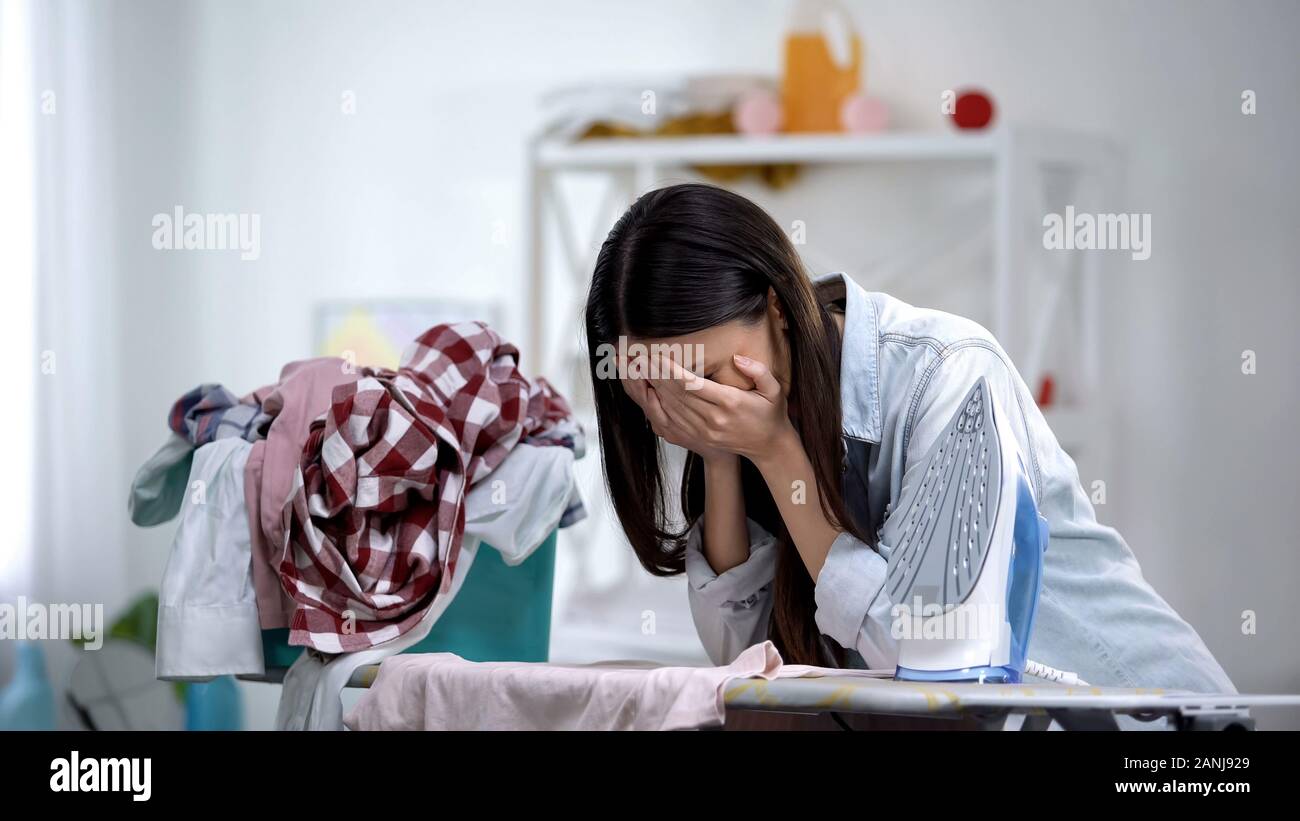 Stressed housewife ironing clothes leaning on board and crying ...