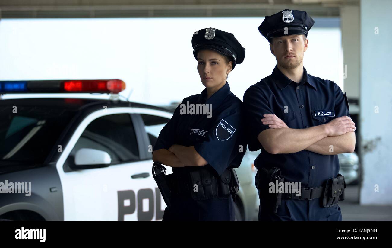 Two brave policemen in uniform and service cap posing near patrol car ...