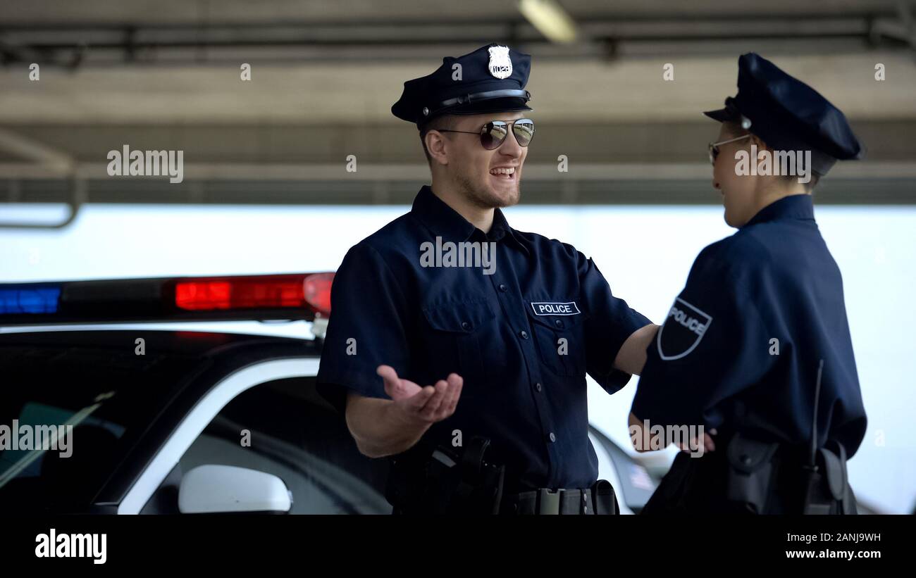 Cheerful police officers laughing standing near car, successful patrol ...