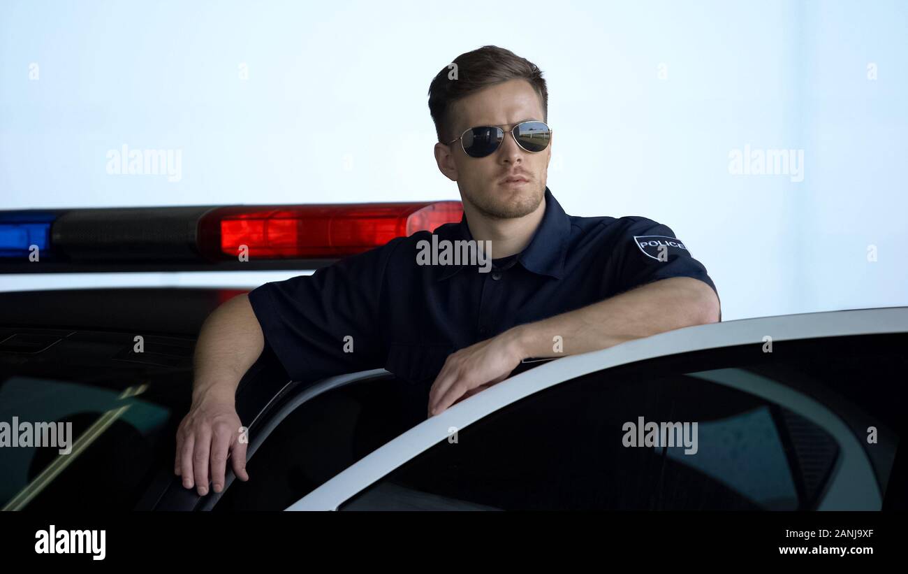 Serious patrol officer in sunglasses monitoring road standing near car ...
