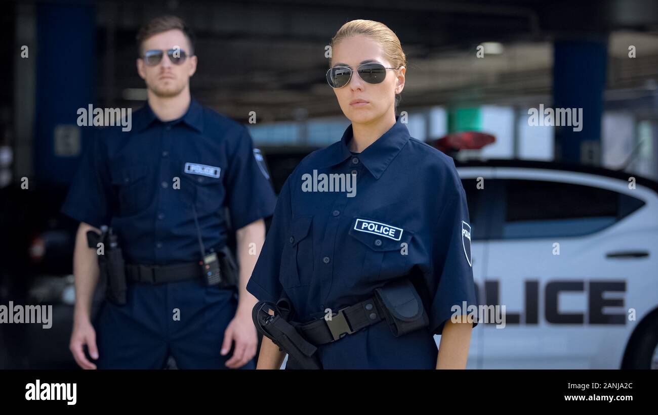 Serious woman and man police officers in sunglasses standing outdoor ...