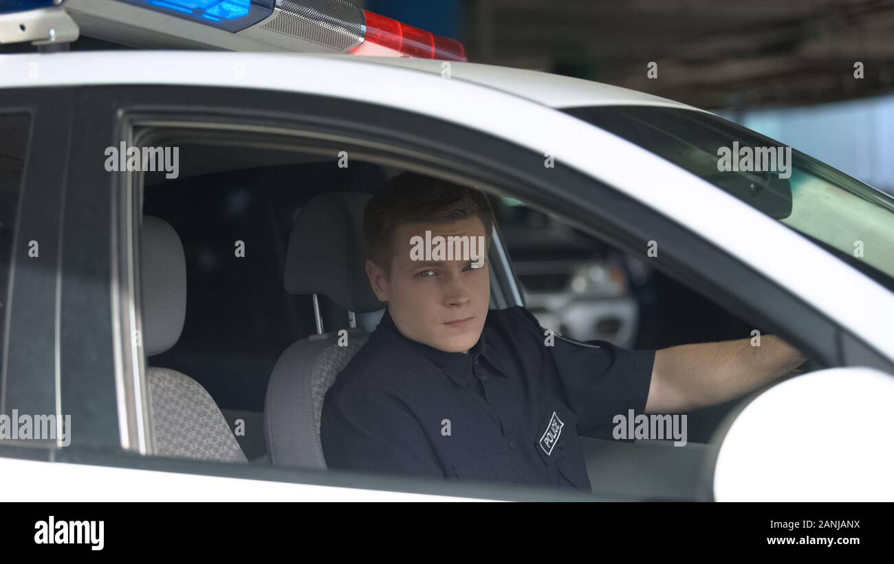 Confident male police officer looking at camera from patrol car ...