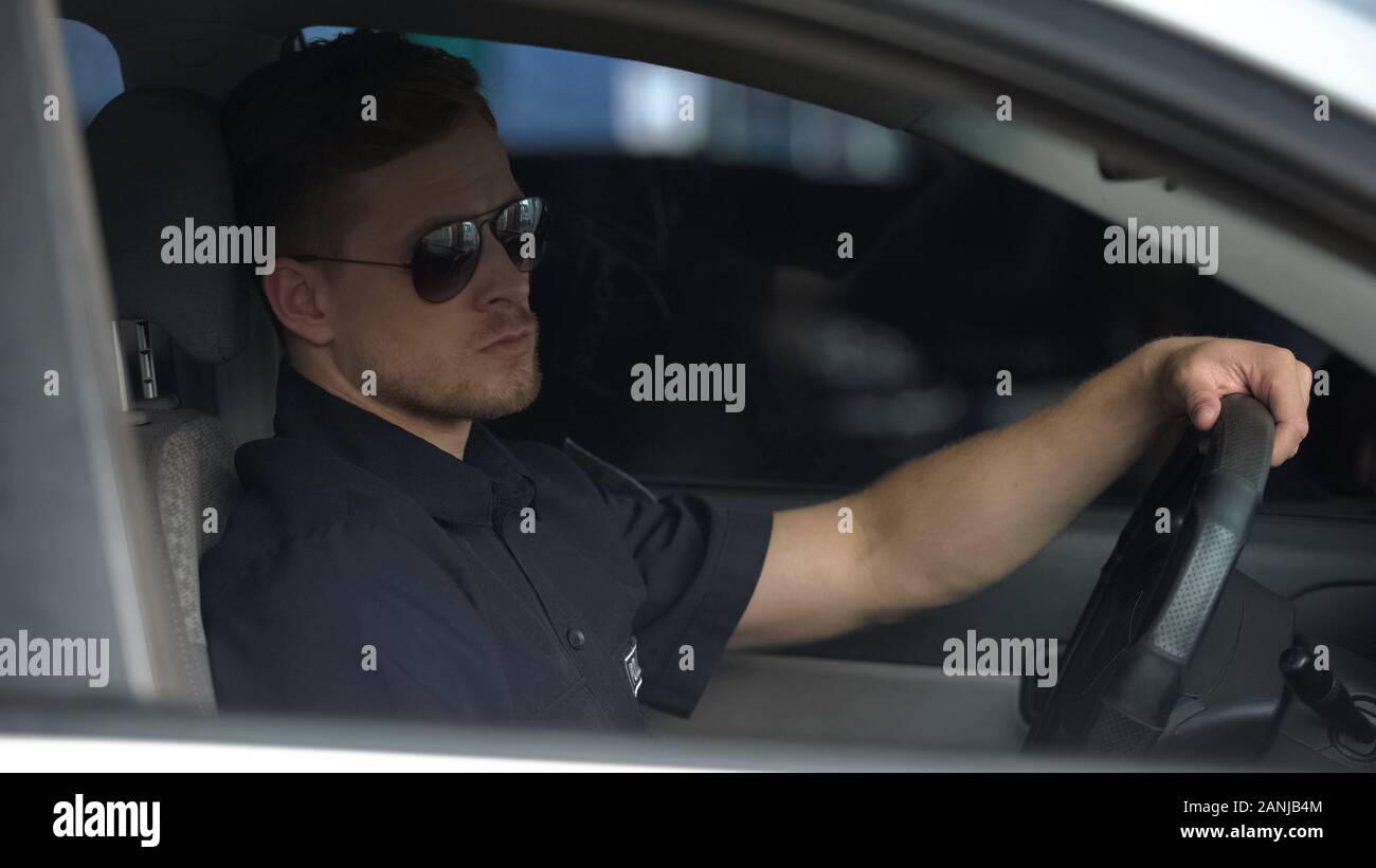 Confident policeman sitting in patrol car and wearing sunglasses, ready ...