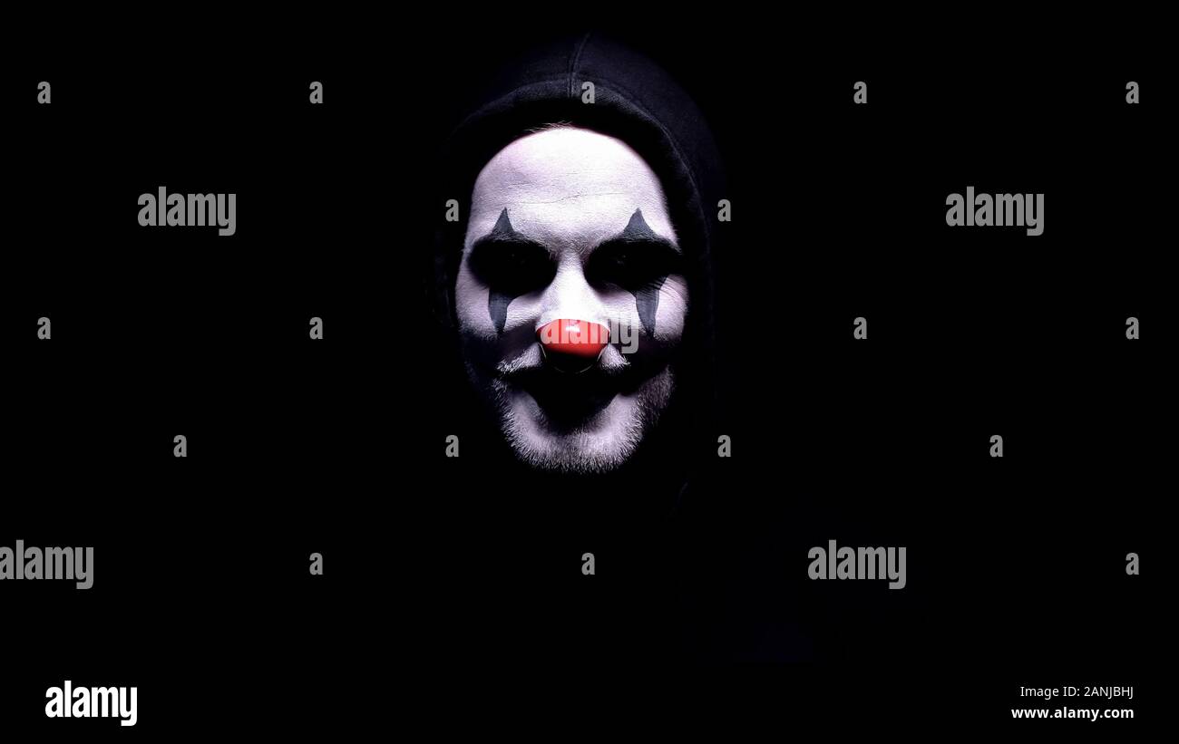Maniac with spooky clown face angrily smiling into camera, psycho ...