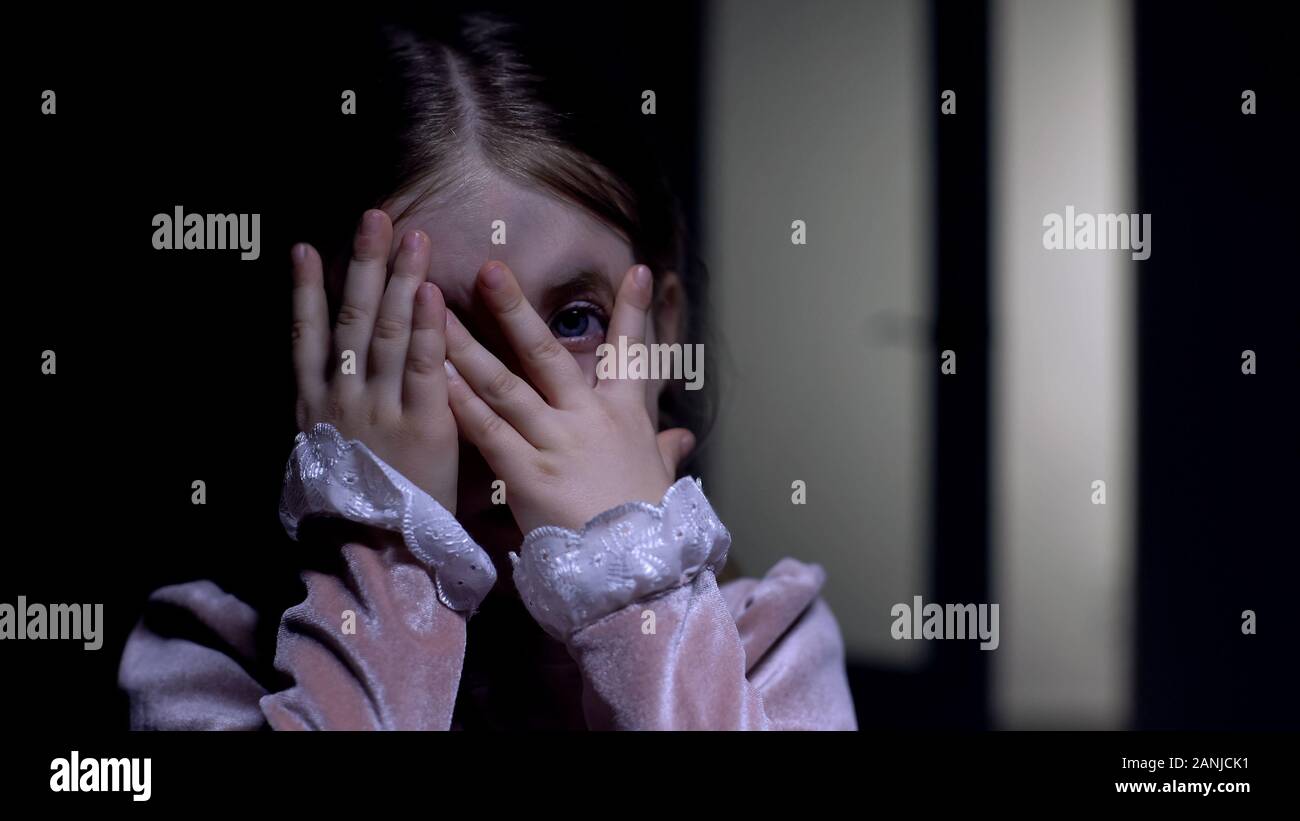 Scared female kid peeping through fingers at camera, phobia and anxiety ...