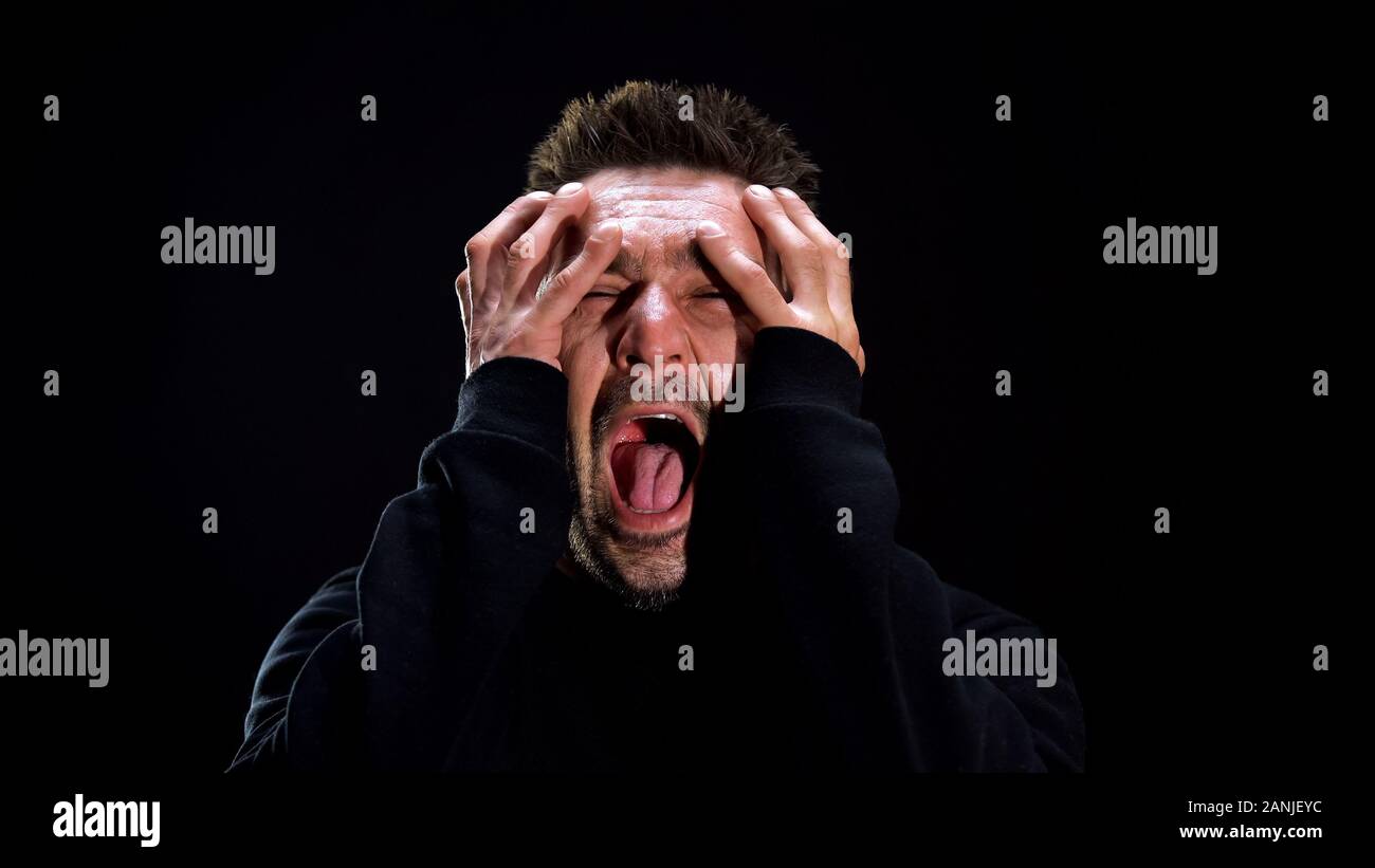 Frightened male shouting on black background, anxious psychopath ...