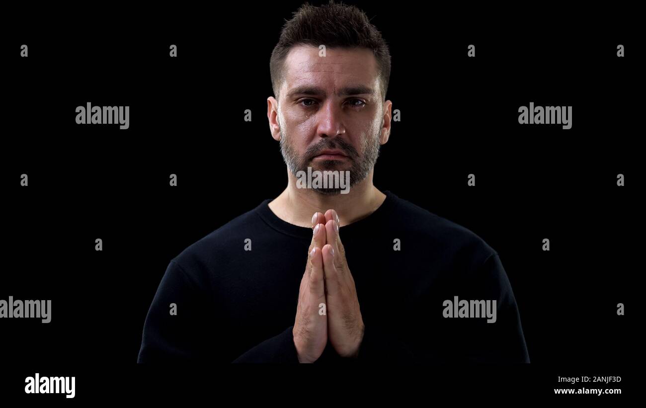 Crying male joining hands and praying on black background, sins ...