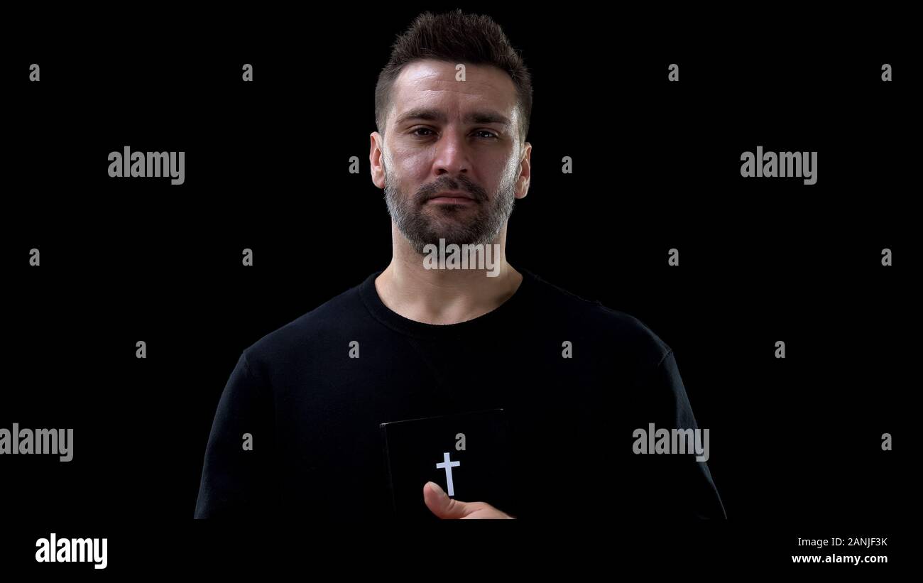 Crying male with bible hands looking camera on dark background, mercy ...