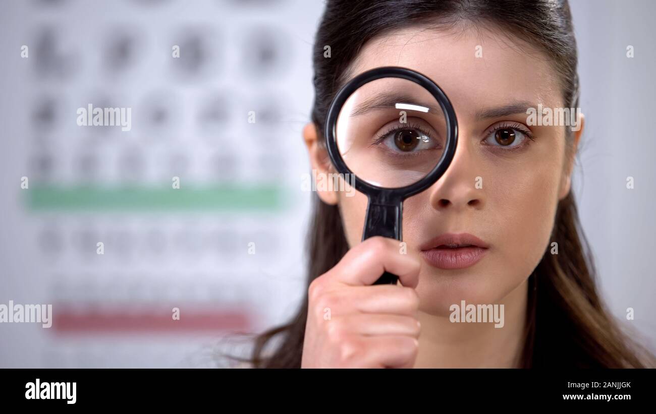 Young woman looking at camera through magnifying glass, vision ...