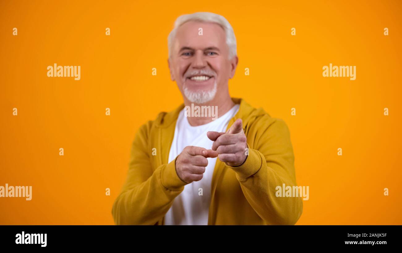 Cheerful pensioner showing hey you gesture, pointing fingers on camera ...