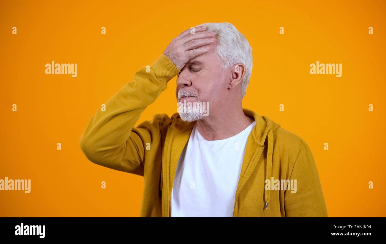 Gray-haired pensioner showing face-palm gesture against orange ...