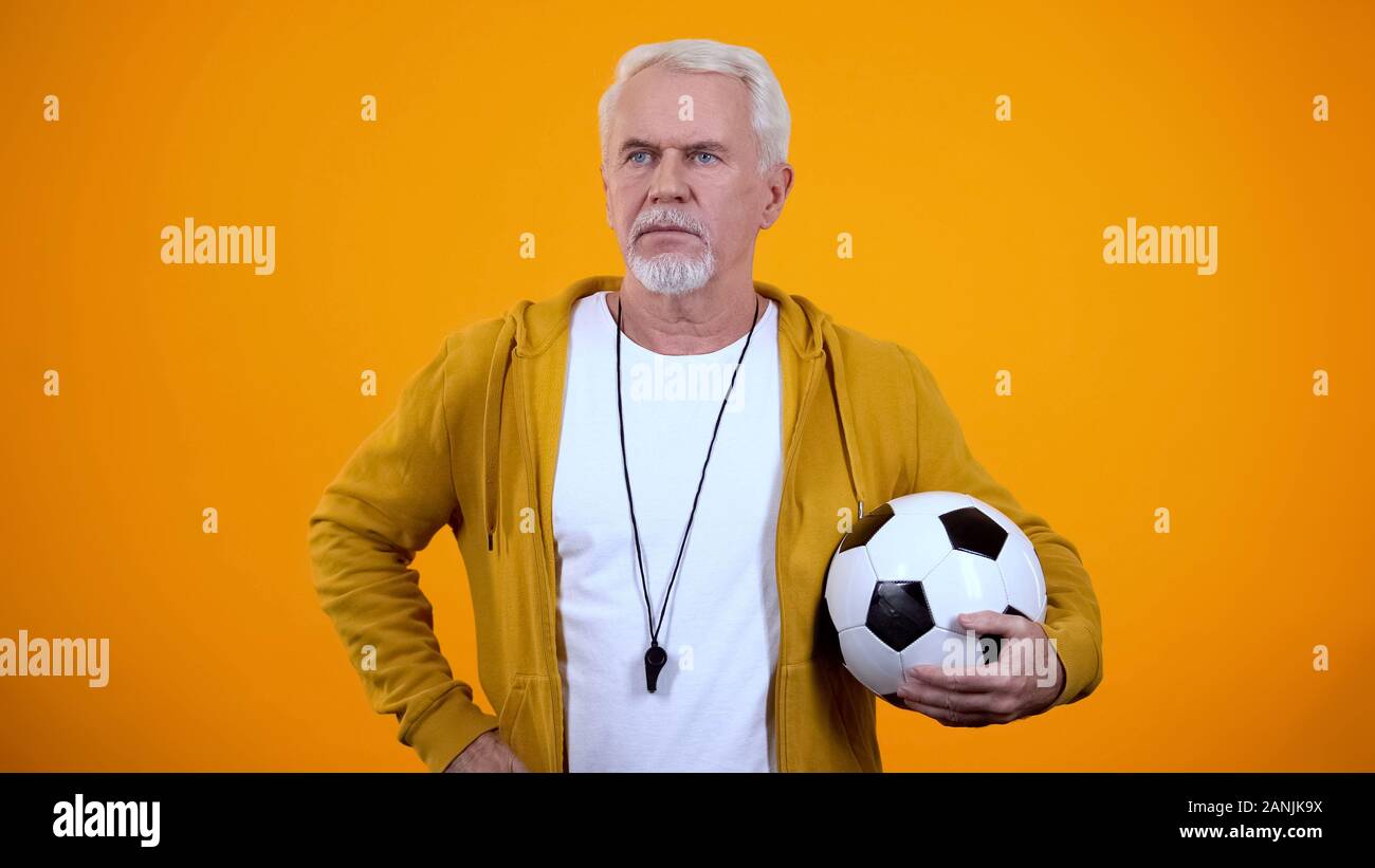 Sad coach with football and whistle watching play, training team before ...