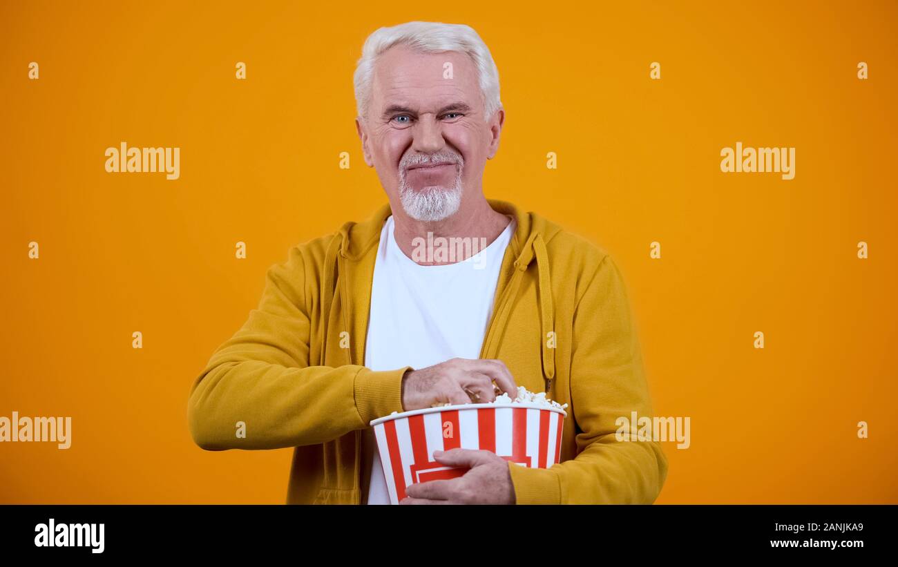 Old man displeased with uninteresting movie, holding popcorn, yellow ...