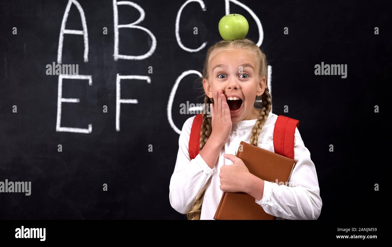 Funny pupil with apple on head standing against blackboard, education ...