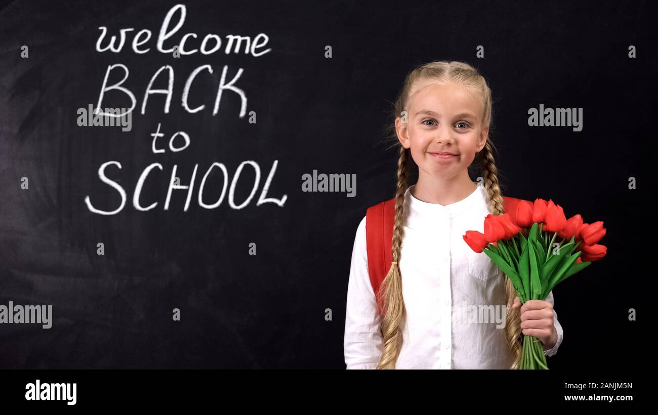 Cute smiling girl holding bunch of tulips near chalkboard welcome back ...