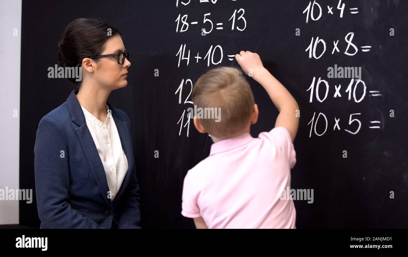 Math teacher checking schoolboy solving exercises writing on blackboard ...
