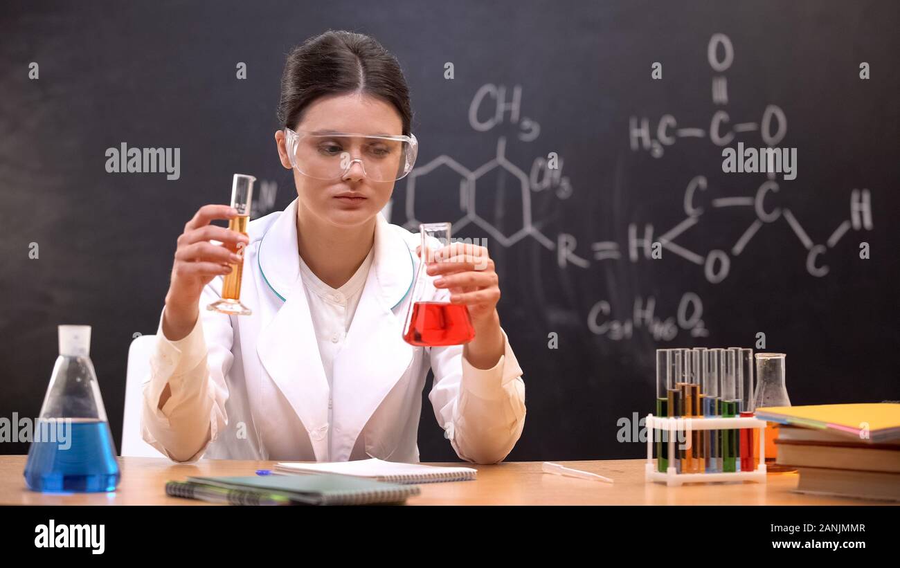 Woman scientist looking at flask with red liquid before adding orange ...
