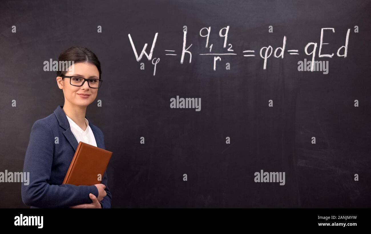 Young clever teacher standing near blackboard and looking to camera ...