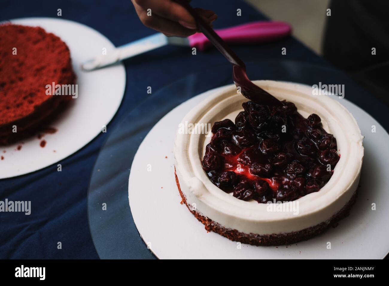 Cook puts jam with berries on the cake with cream. The pastry chef puts ...