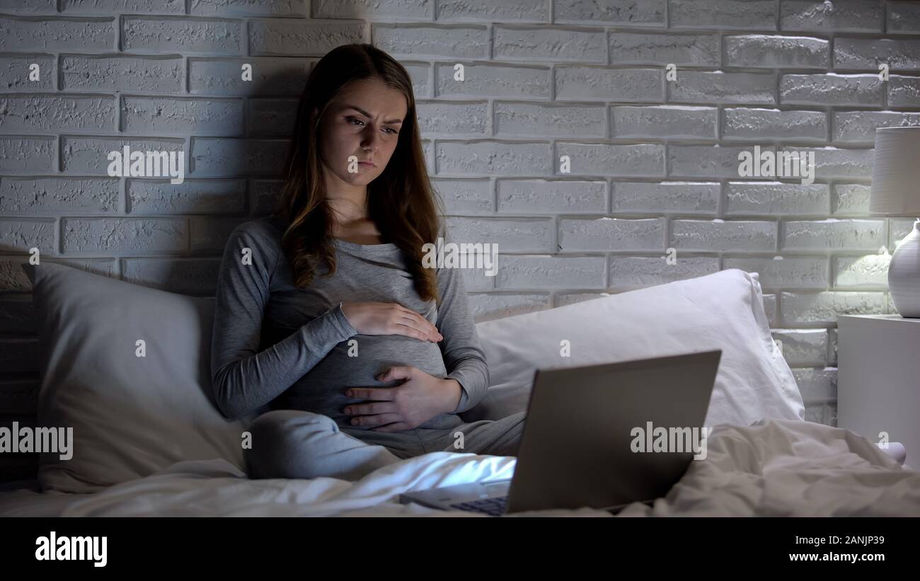 Sad pregnant woman holding belly, sitting in front of laptop, life ...