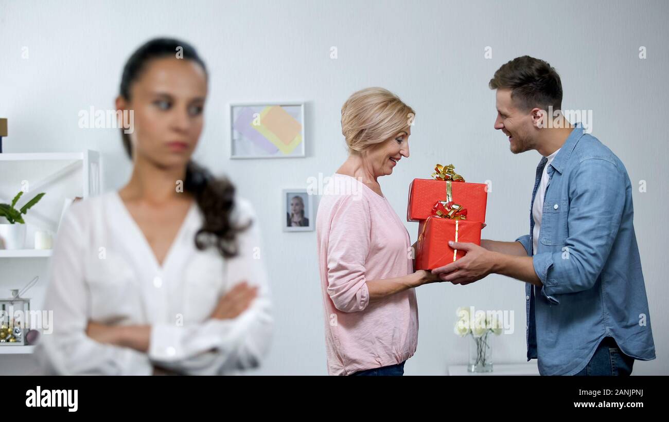 Husband presenting gifts to mother, upset wife with hands crossed ...