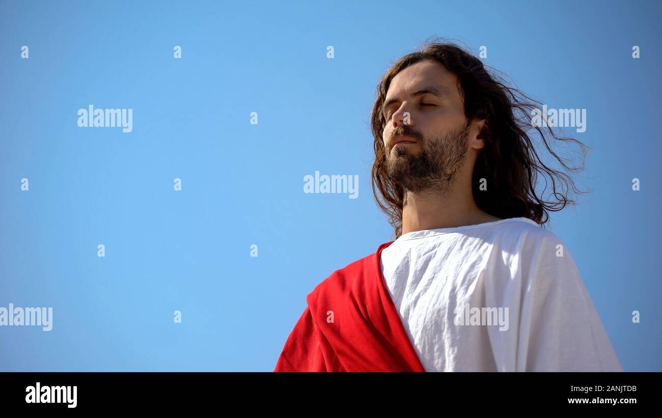 Saint man with closed eyes praying to god on blue sky background ...