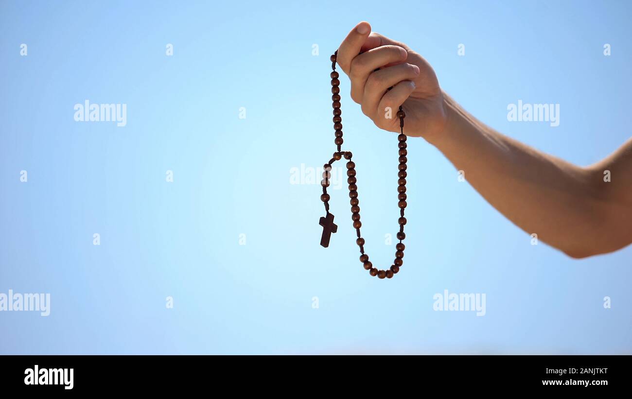 Hand holding rosary, praying to god on blue background, religious ...