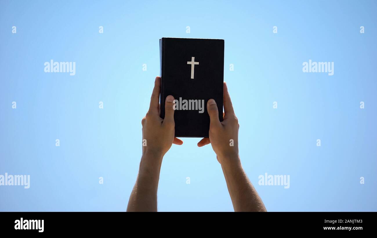 Man reaching out hands to sky holding bible, new testament, ten ...